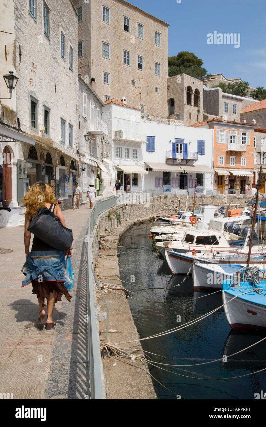 A woman carries shopping along the pretty harbourfront of Hydra Town ...