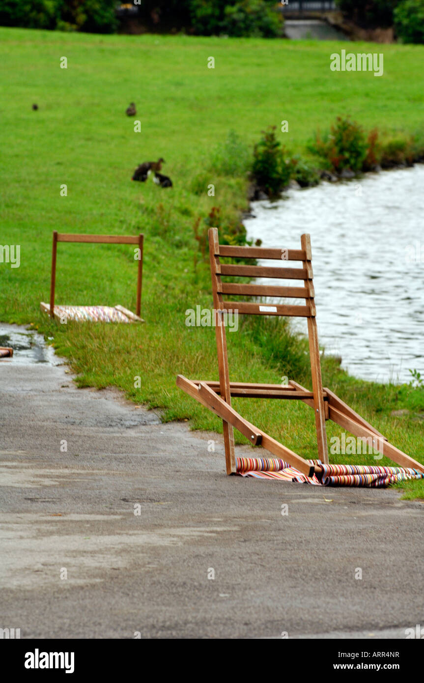 collapsed deckchairs by the side of a lake in the summer on a windy ...