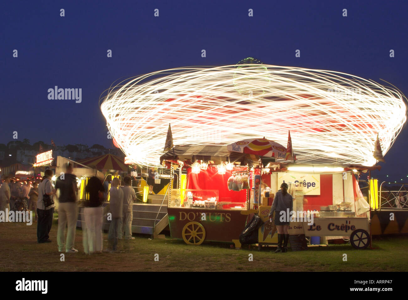 A long exposure of a fairground at night showing the lights as the ride ...