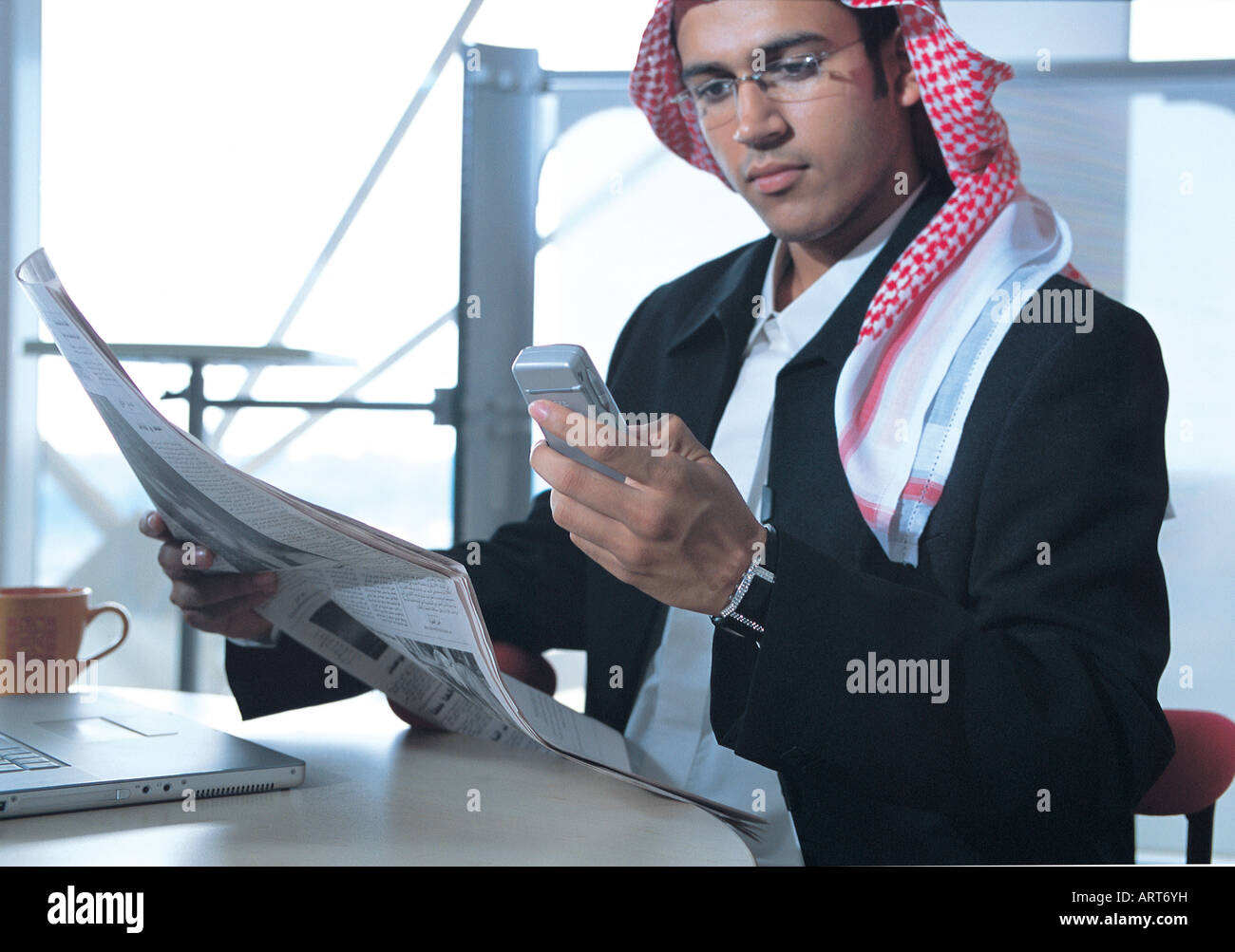 Saudi Arabian businessman reading newspaper and checking mobile phone ...