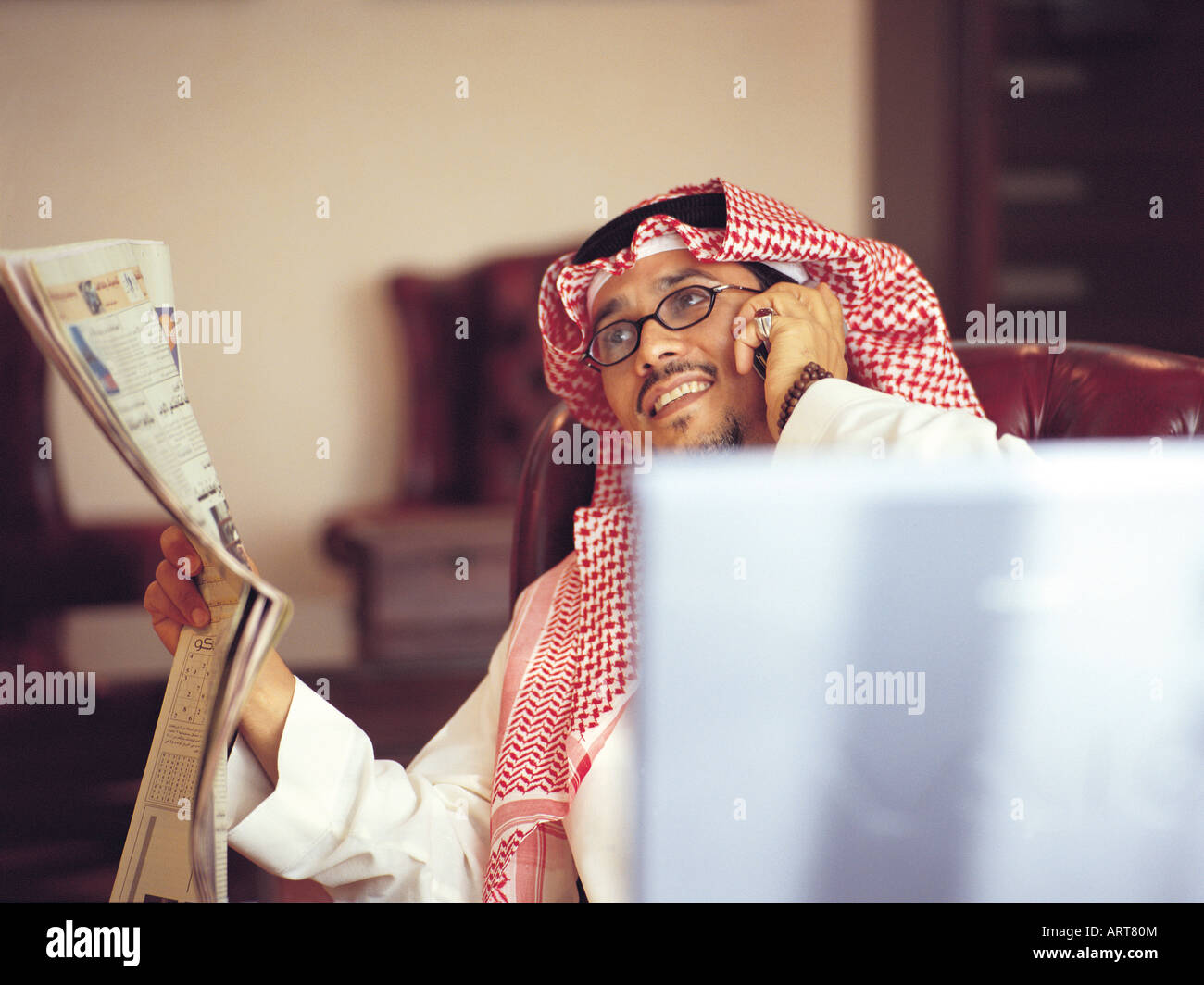Saudi businessman reading Arabic newspaper and using mobile phone Stock ...