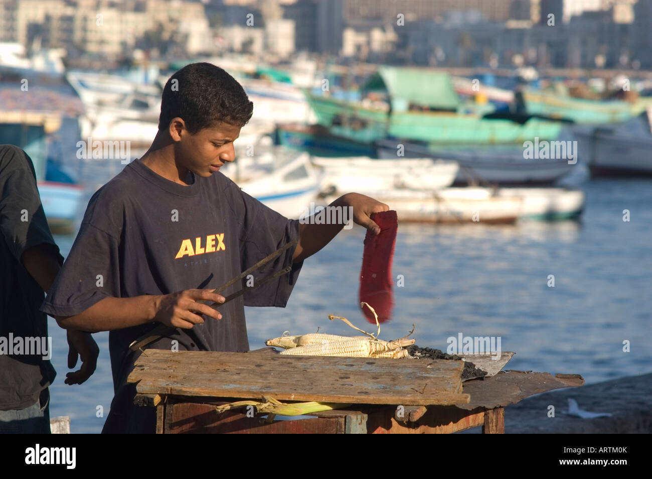 Egyptian man grilling corn on the cob over charcoal on the sidewalk ...