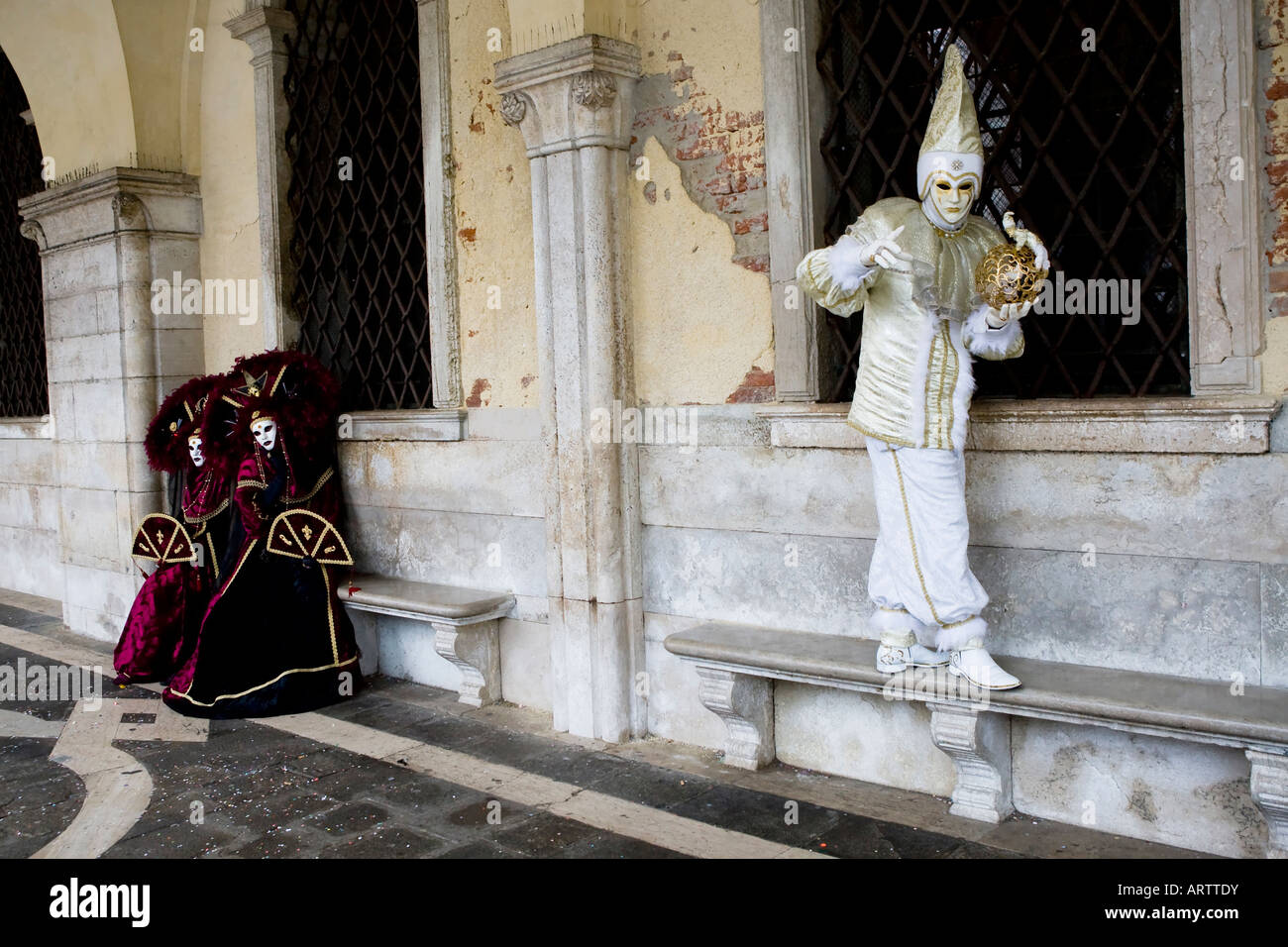 A man in Carnival Costume and mask balancing on a stone bench being ...
