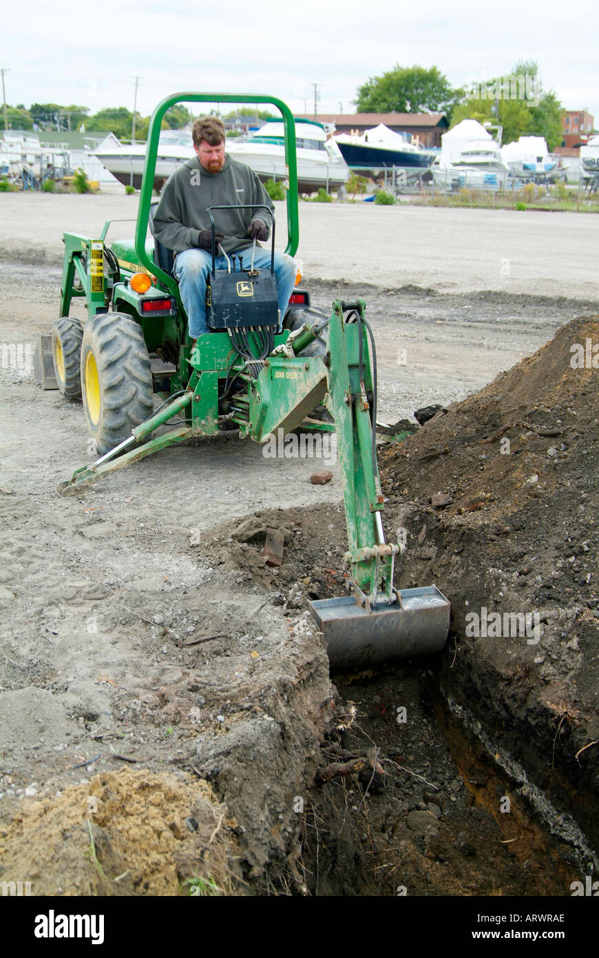 Adult male construction worker uses back hoe to dig a trench to lay ...