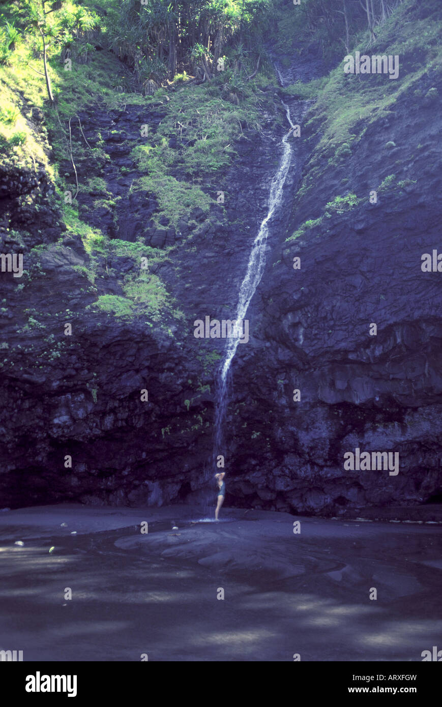 Beautiful young woman stands beneath cascading oceanfront waterfall at ...