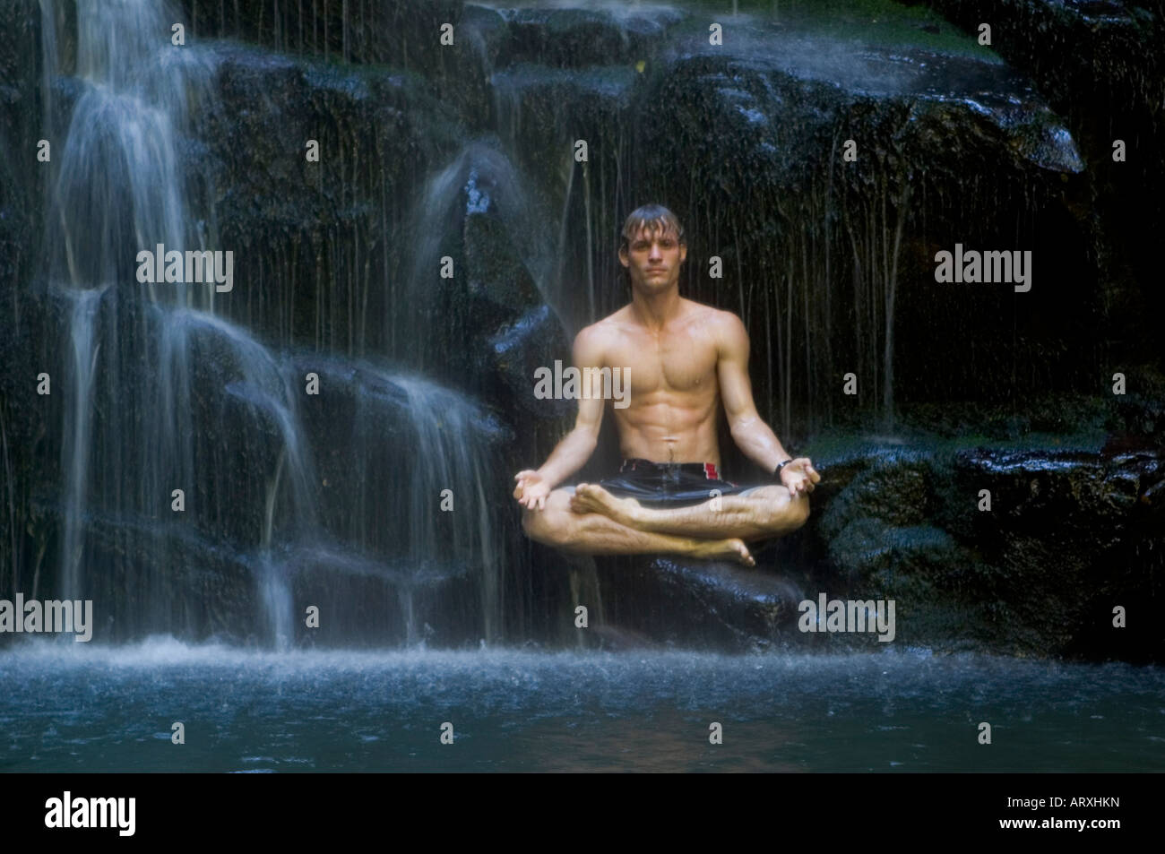 Man relaxes in meditation position under a waterfall Stock Photo - Alamy