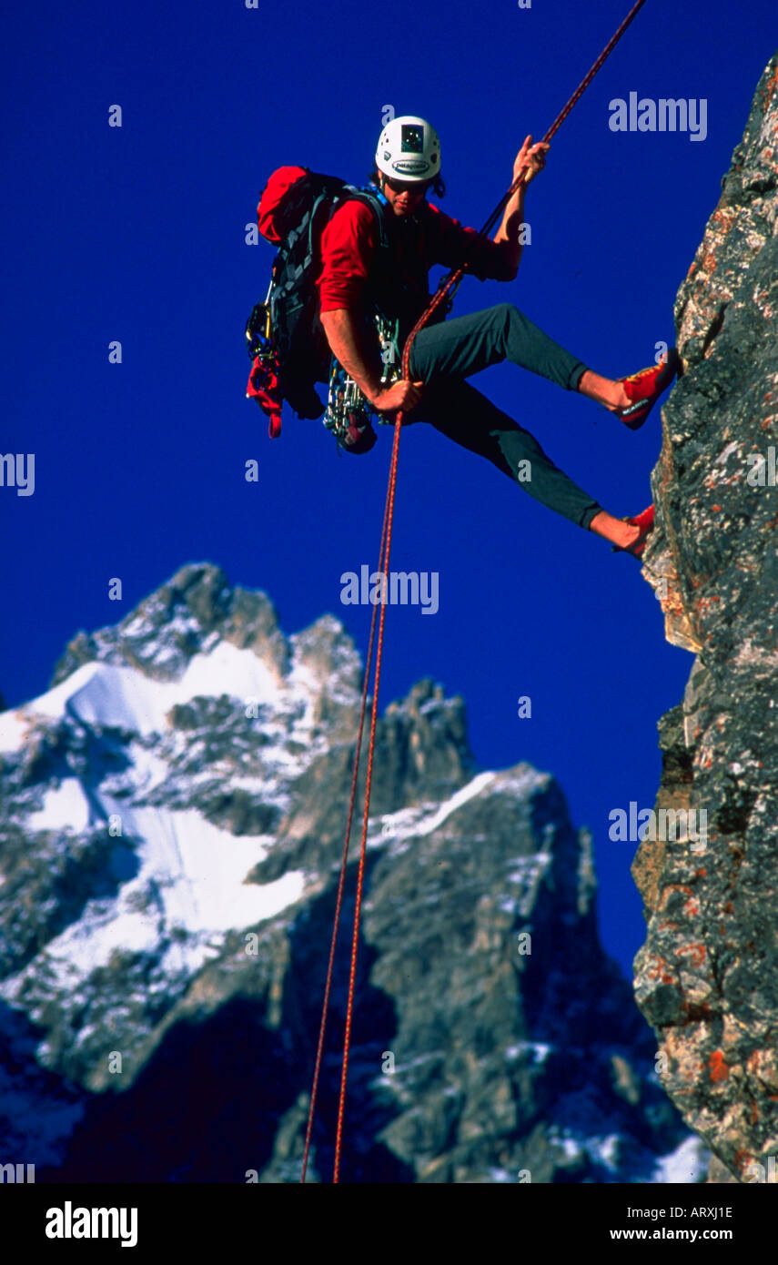 Man wearing helmet and rock climbing gear uses ropes to repel down a ...