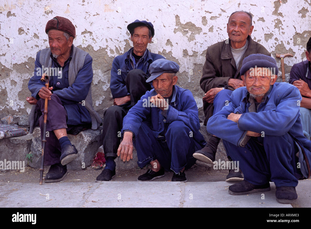 Chinese men squatting against the wall at lake Erhai village near Dali ...