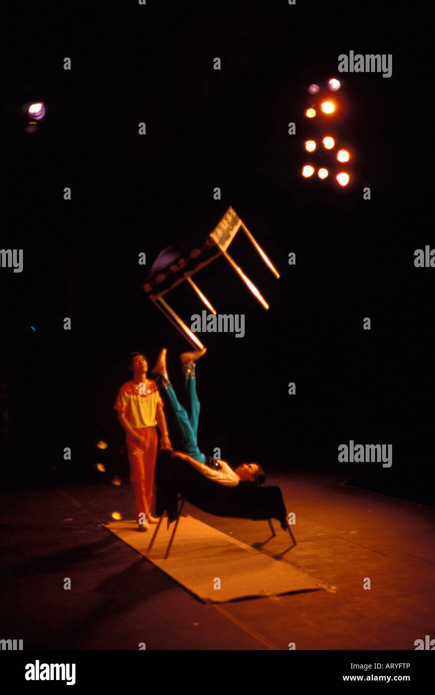 Chinese acrobatic act, girl lying on back balancing an upright table on ...
