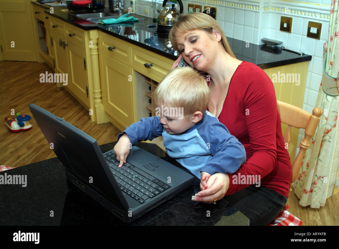 Young mother using laptop computer and telephone in kitchen Helping ...