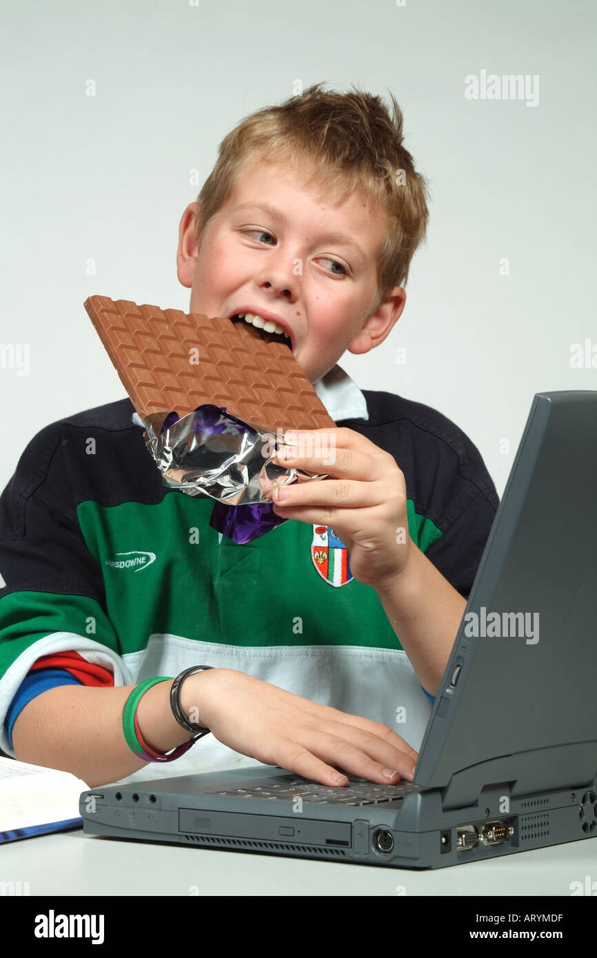 schoolboy using laptop computer. Boy eating a large bar of chocolate ...