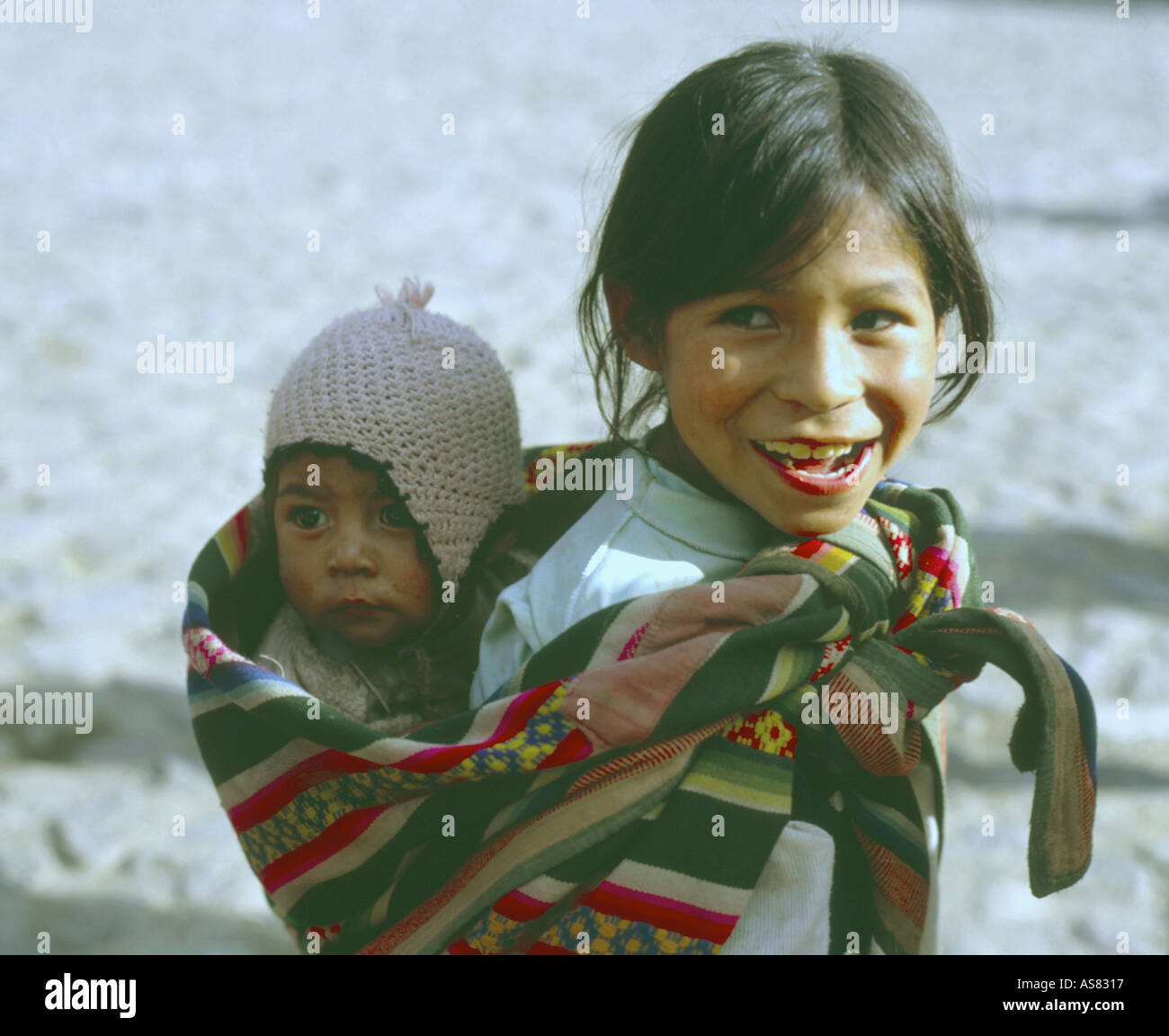 Smiling young Andean girl carrying baby with knitted bonnet, wearing ...