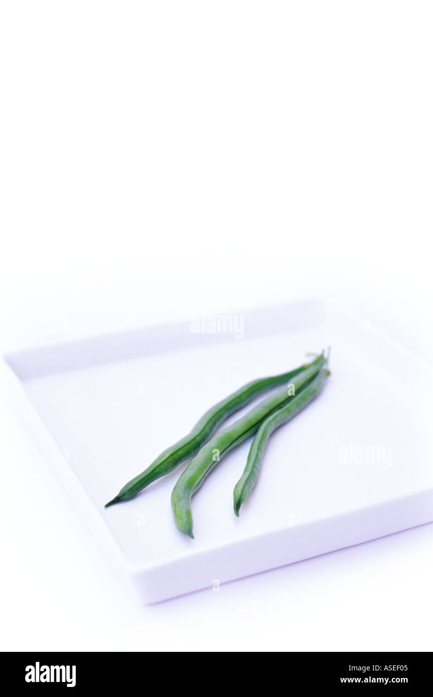 Green fresh string beans tantalisingly hanging over a set of square ...
