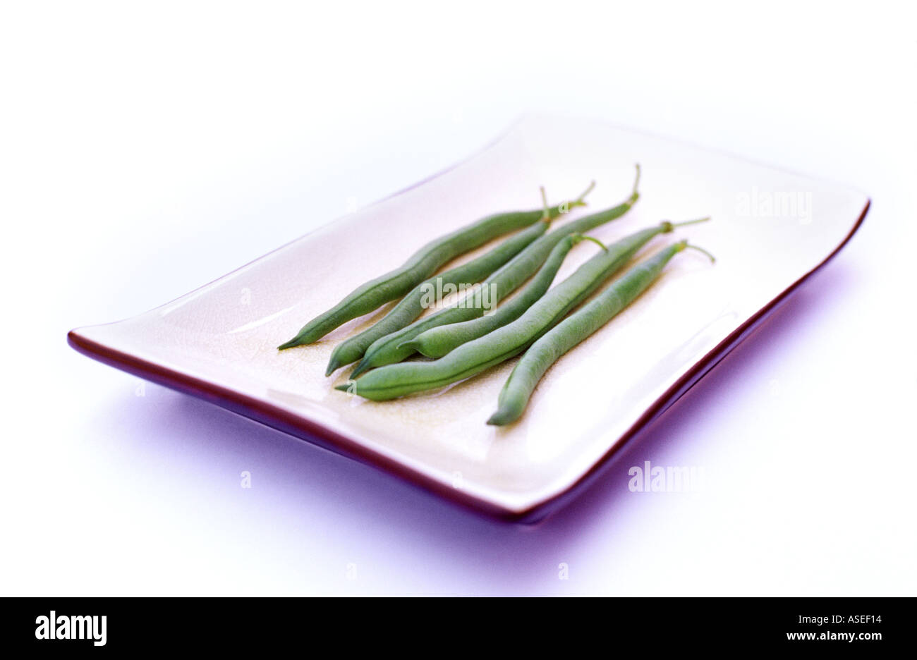 Green fresh string beans laid out on rectangular plate against clean ...