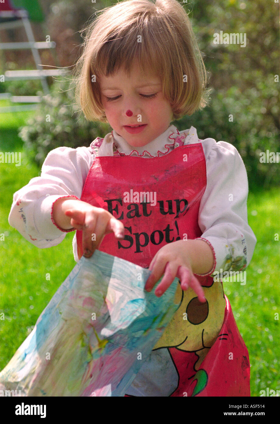 child with a painting, wearing a painting apron and with paint on her ...