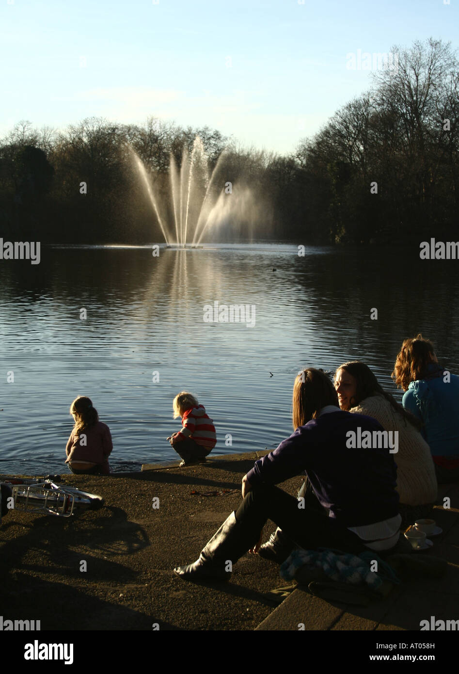 Group of young people includoing children sitting by lake and fountain ...