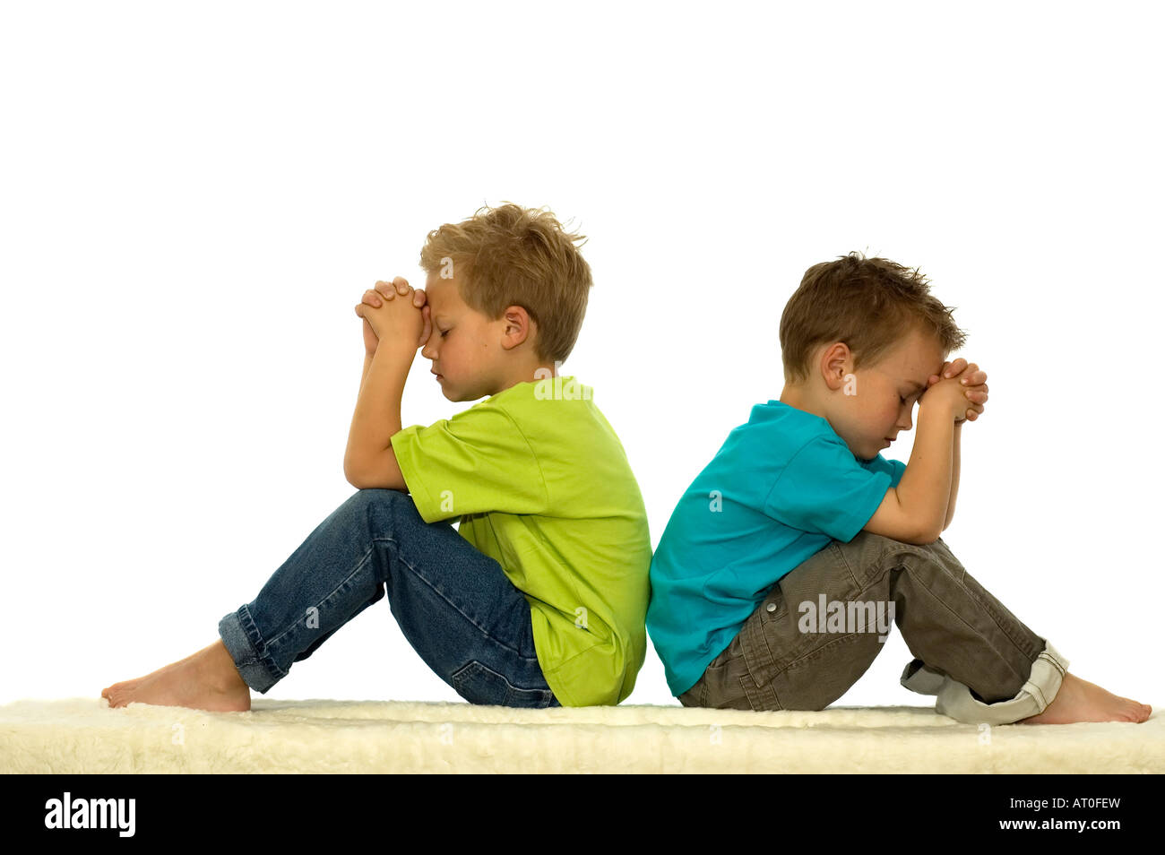 Two friends are praying while sitting with their backs against each ...