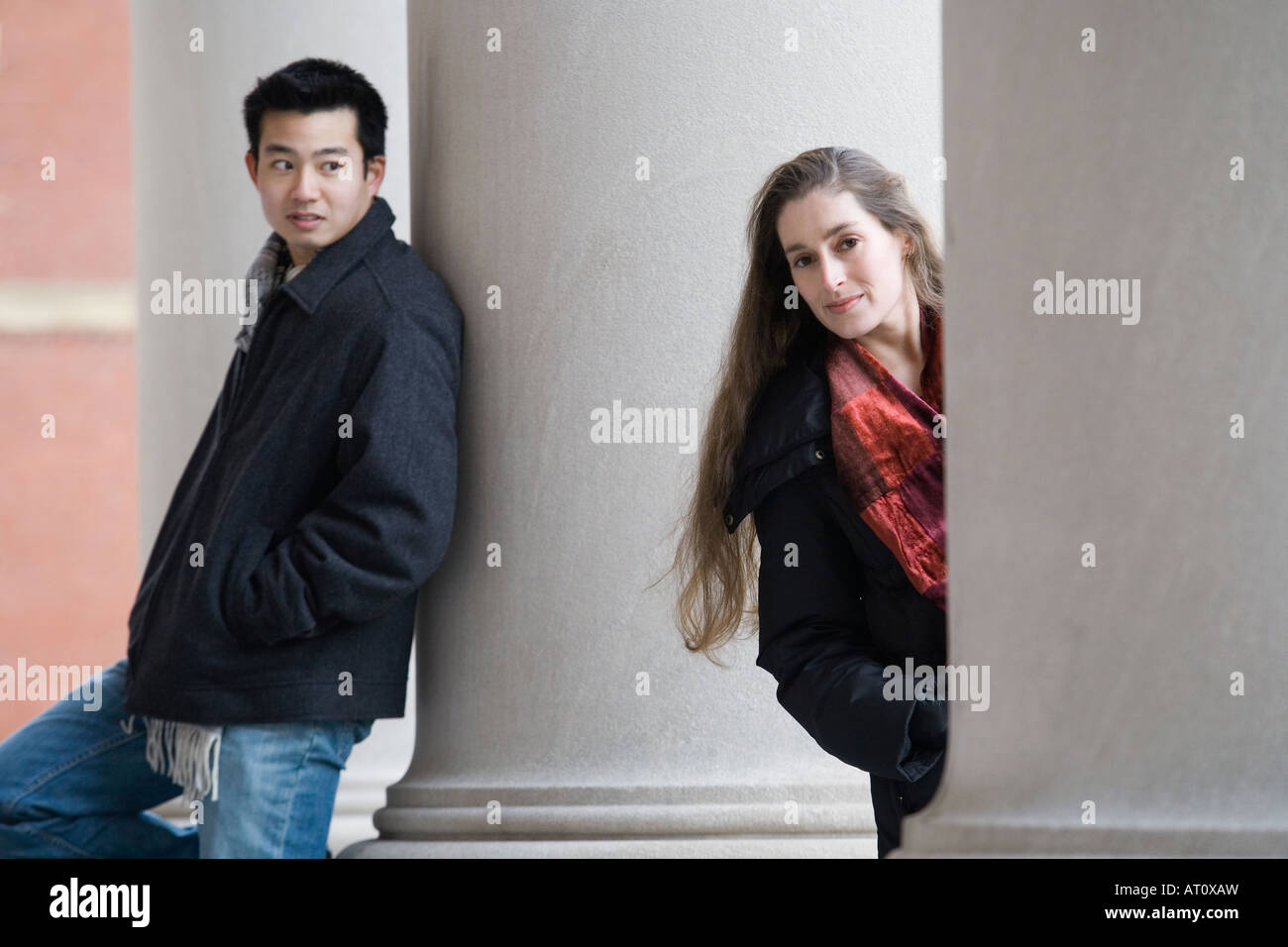 Portrait of a young woman peeking from behind a column and a young man ...