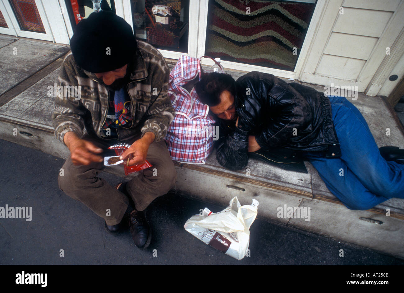 Two homeless men outside sitting and lying on city street pavement ...