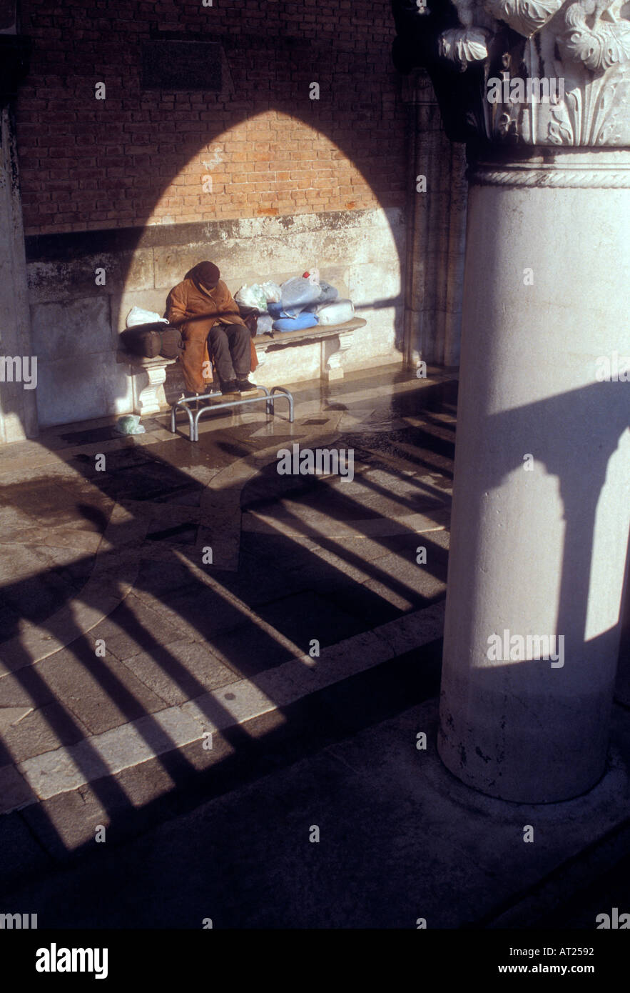 Elderly homeless man seated with his worldly possessions framed by ...