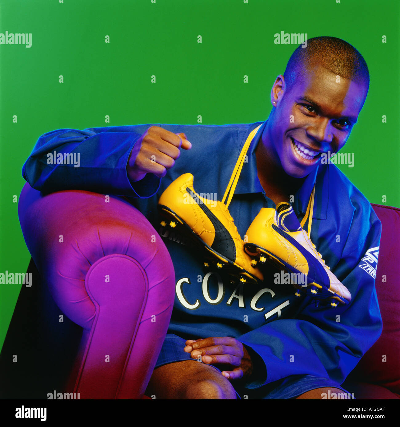 A man sitting on a sofa with a pair of football boots around his neck ...