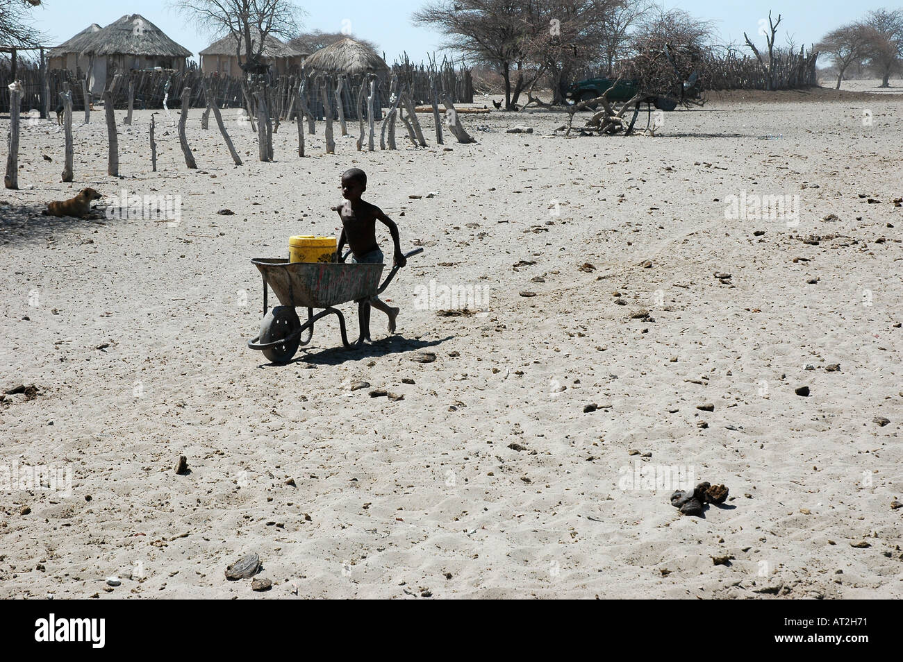 Young boy pushing wheel barrow across sand in village in Botswana ...