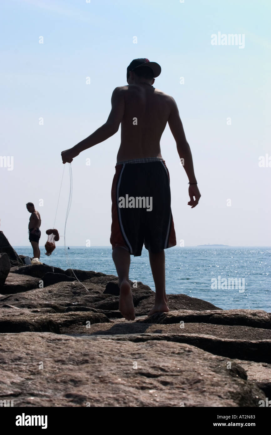 Teen boy using string to fish from the rocks at the beach Stock Photo ...