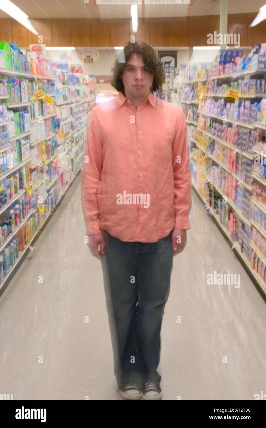 Teen boy standing in the middle of a food aisle at a grocery store ...