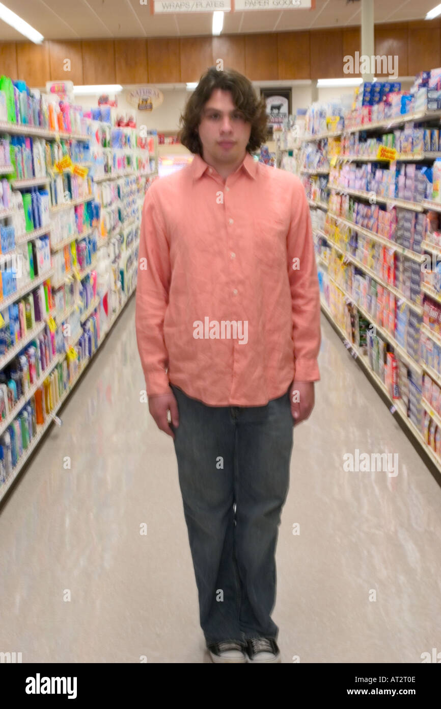 Teen boy standing in the middle of a food aisle at a grocery store ...