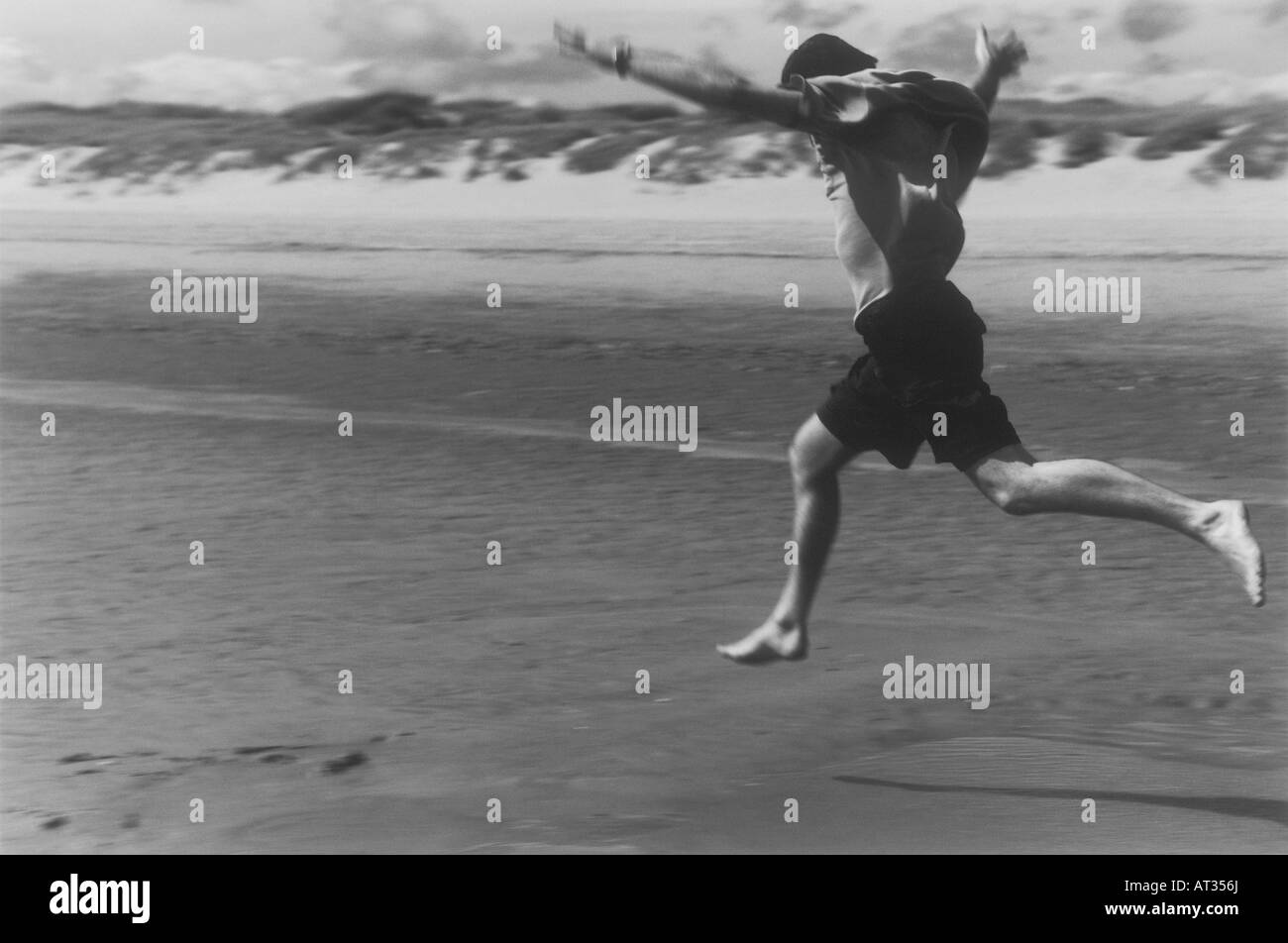 A man running a long a beach, jumping arms stretched out Stock Photo ...