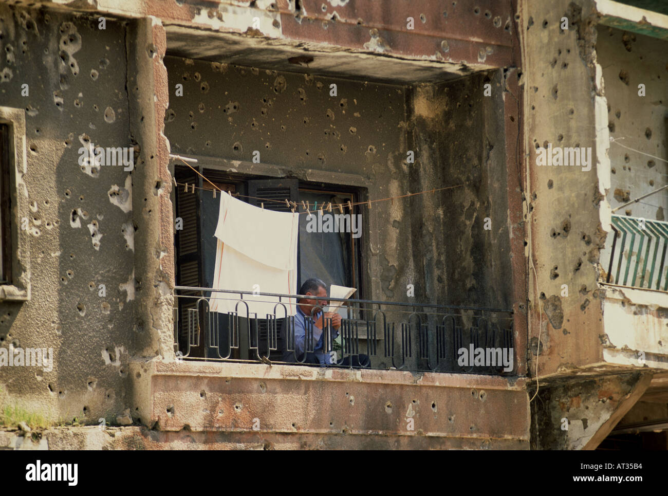 Lebanese man reading newspaper on balcony of bullet riddled apartment ...