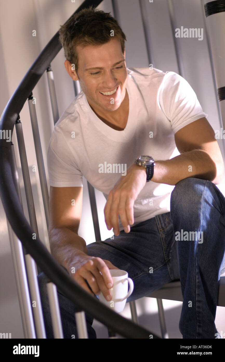 A man sitting on some steps holding a cup smiling Stock Photo - Alamy