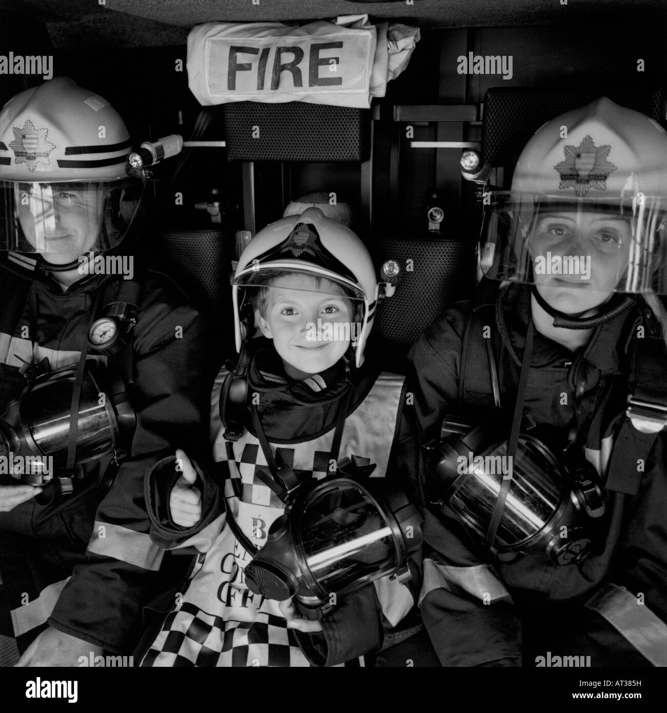 A boy sitting in a fire engine with two firemen Stock Photo - Alamy