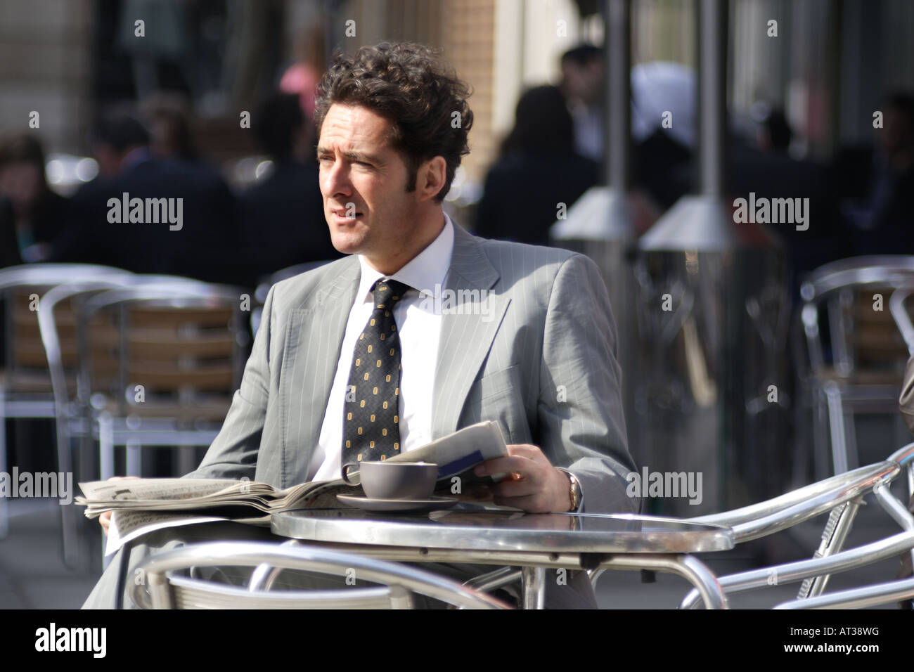 A man sitting outside a café holding a newspaper, thinking/dreaming ...
