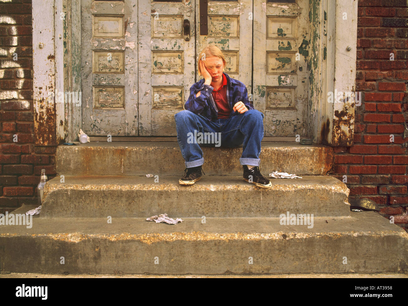 Sad runaway boy sitting on the steps of an abandoned urban building ...
