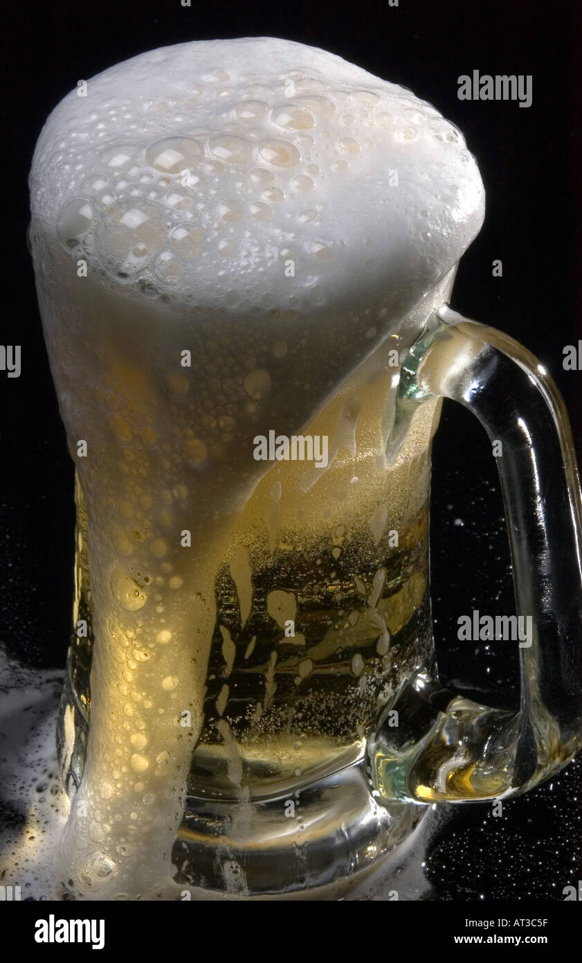 Glass beer mug overflowing foam onto black reflective surface Stock ...