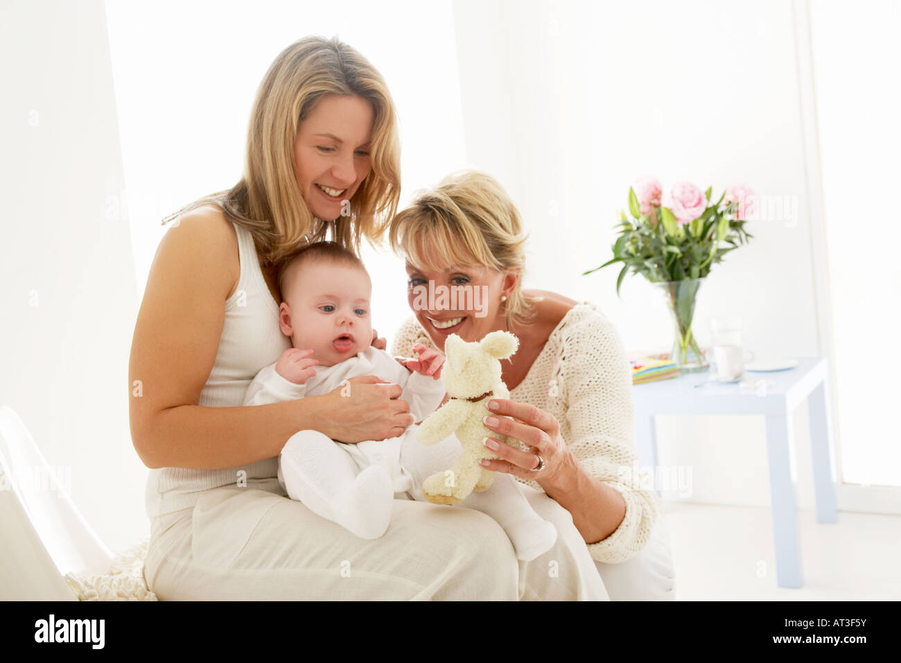 Baby sitting on mother's knee, grandmother holding cuddly toy Stock ...