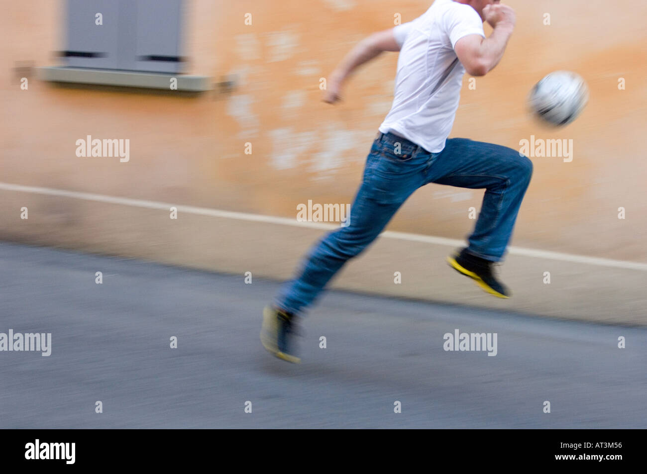 Man running with soccer ball in street Stock Photo - Alamy