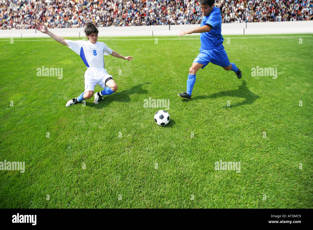 Soccer player kicking ball as defender slides in Stock Photo - Alamy