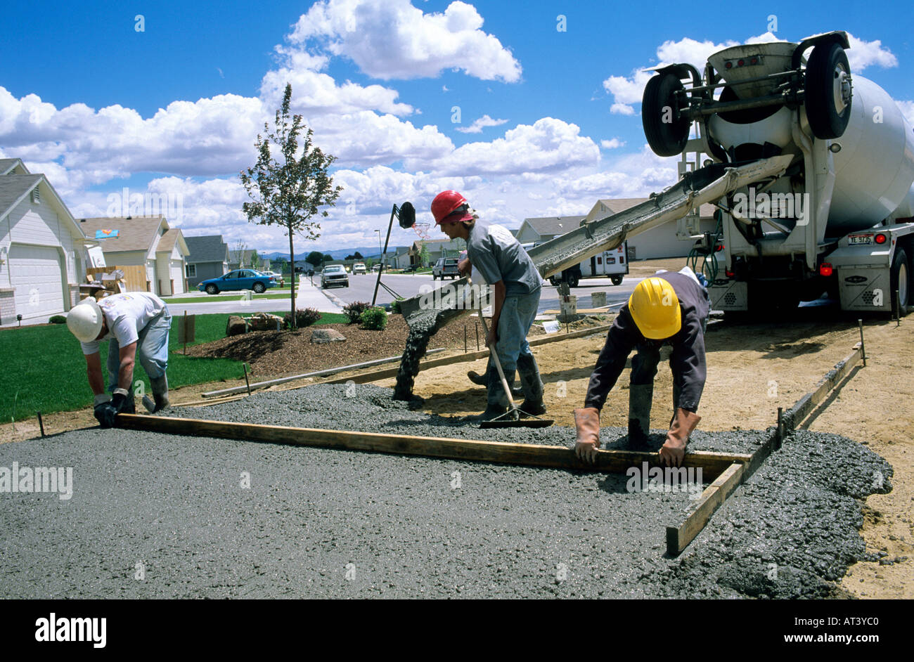 Workers pouring concrete and screeding it to make a driveway in a ...