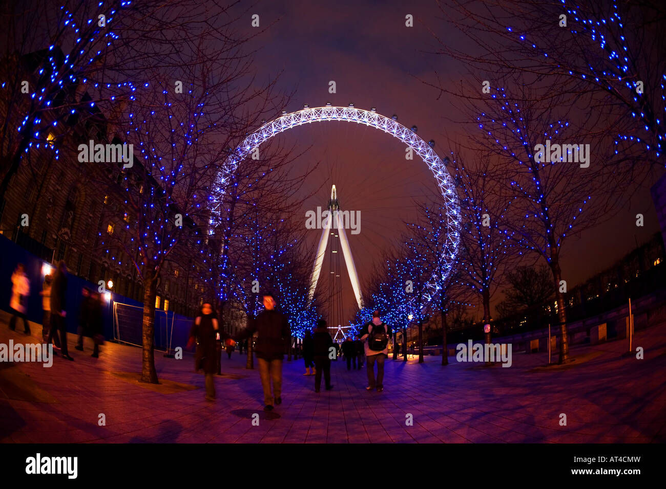 Pedestrians near the London Eye illuminated at night with blue lights ...