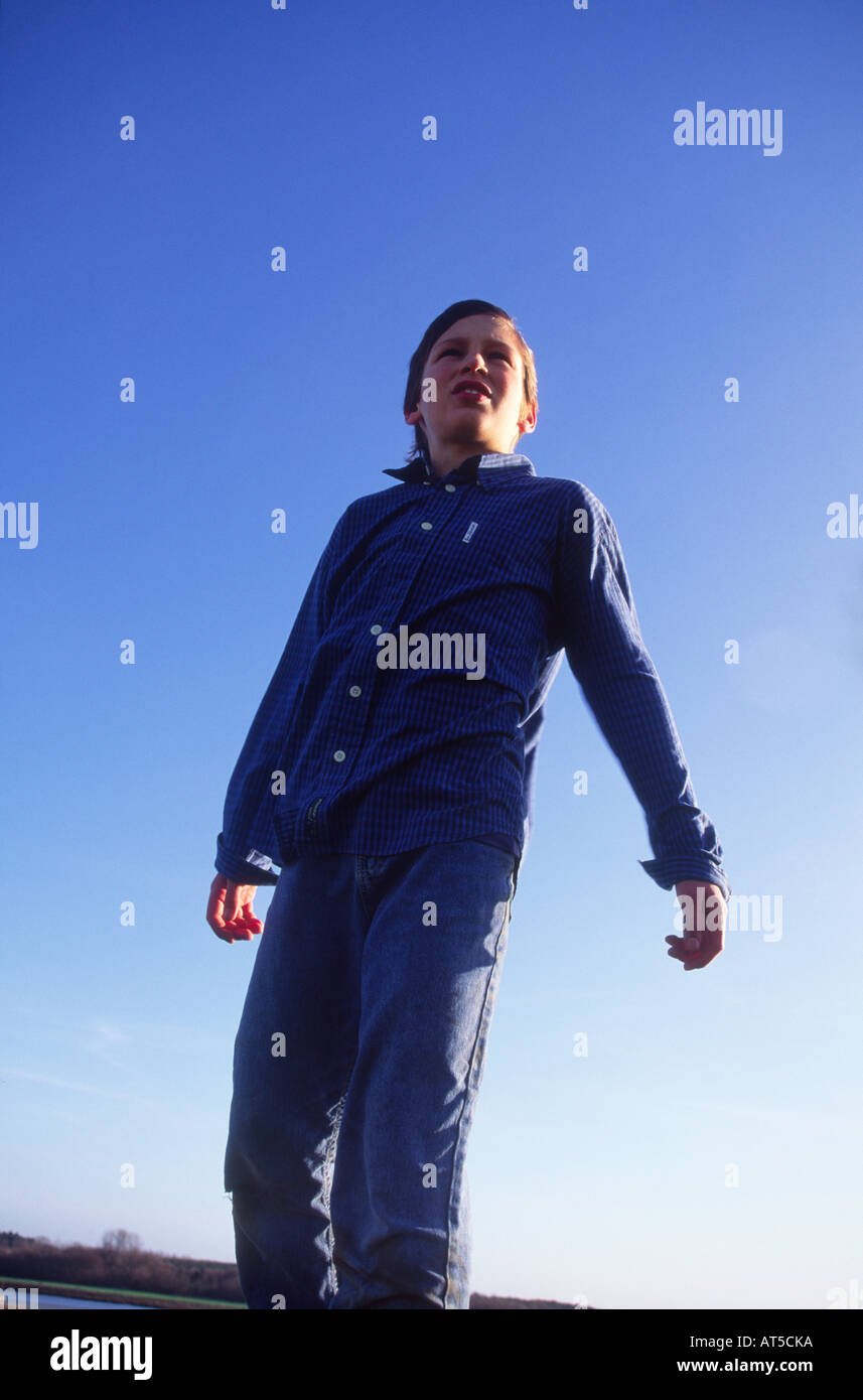 Boy wearing blue against blue sky looking into the distance low angle ...