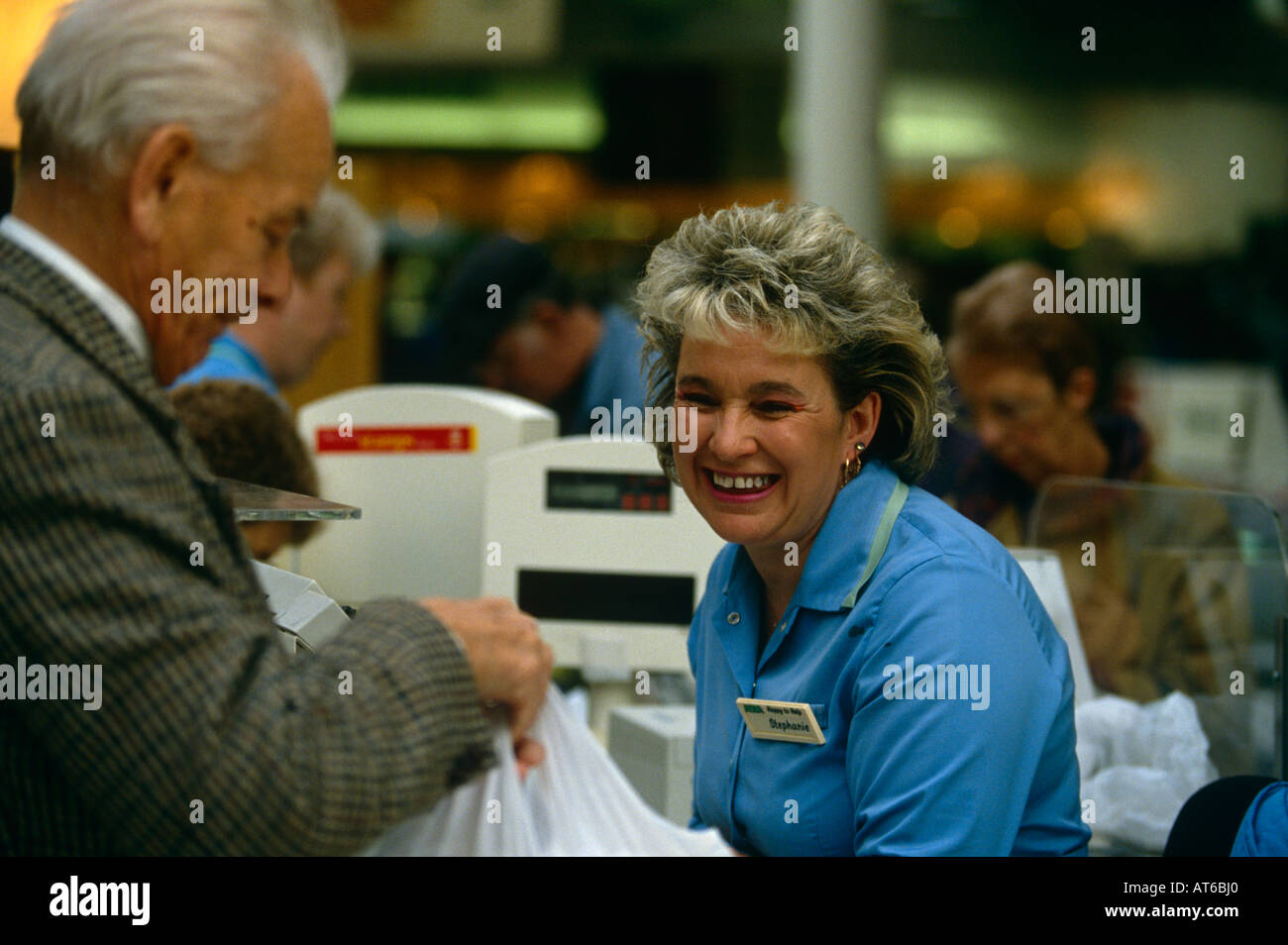 A female cashier smiles and laughs as a man packs his bag at the ...