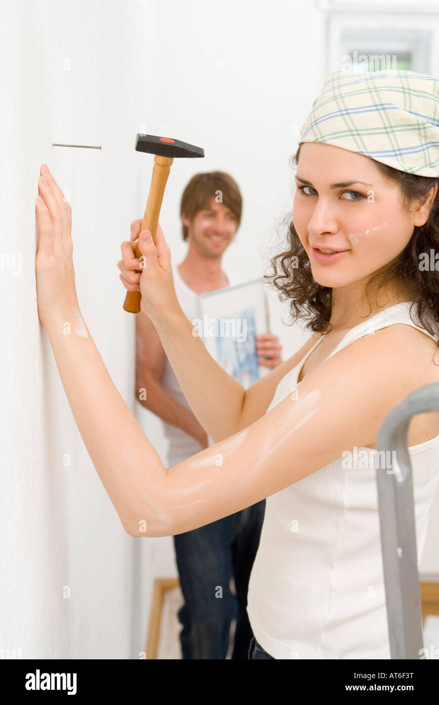 Young woman hammering picture hook on wall, side view Stock Photo - Alamy