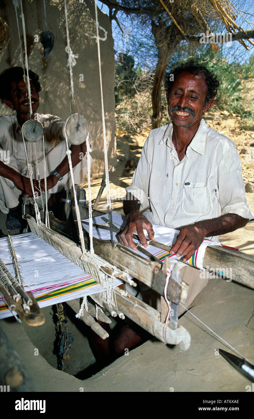 A smiling male weaver working a traditional pit loom in the desert town ...