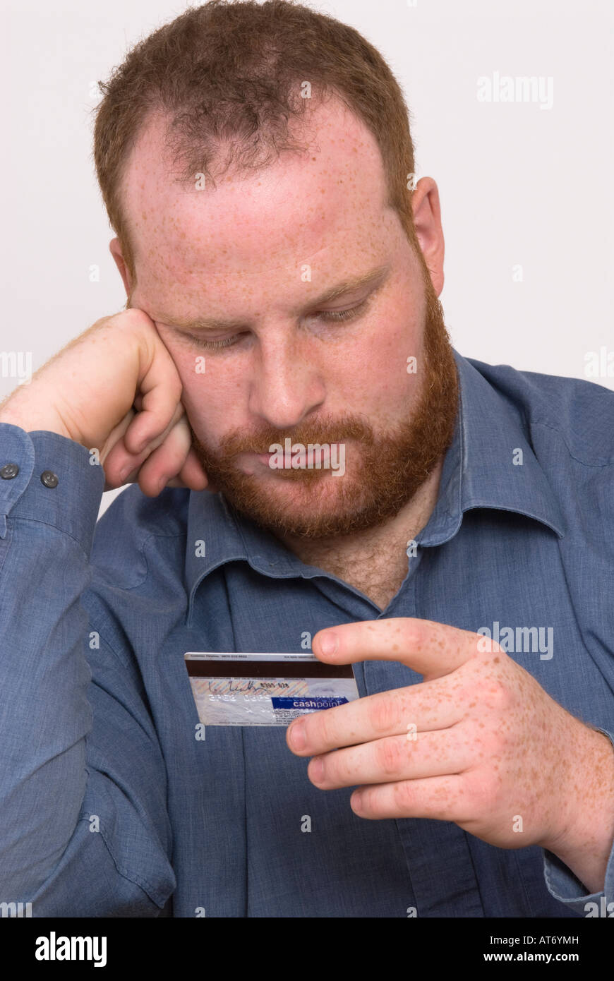 young man looking at and thinking about his credit debit bank card ...