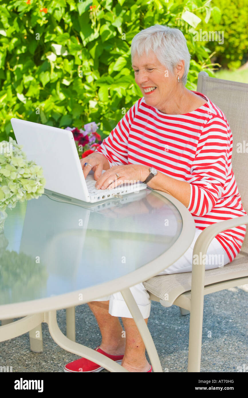 Mature woman working outside on a patio table with her laptop computer ...