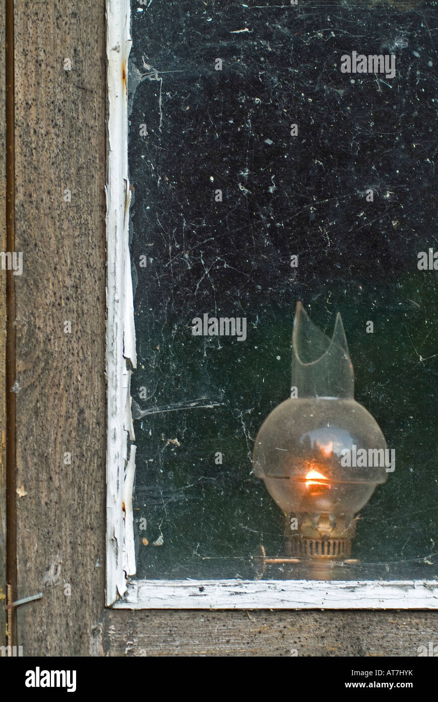 old oil lamp with broken glass burning at window of a timber wooden ...