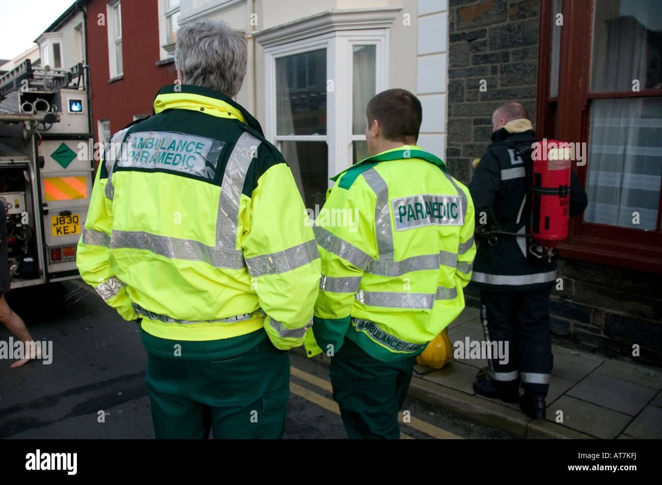 Two paramedics and fireman attending scene of house fire waiting to see ...