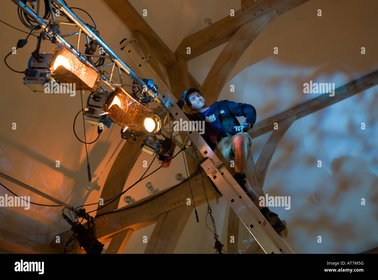 Male lighting rigger on ladder adjusting lights on gantry for ...
